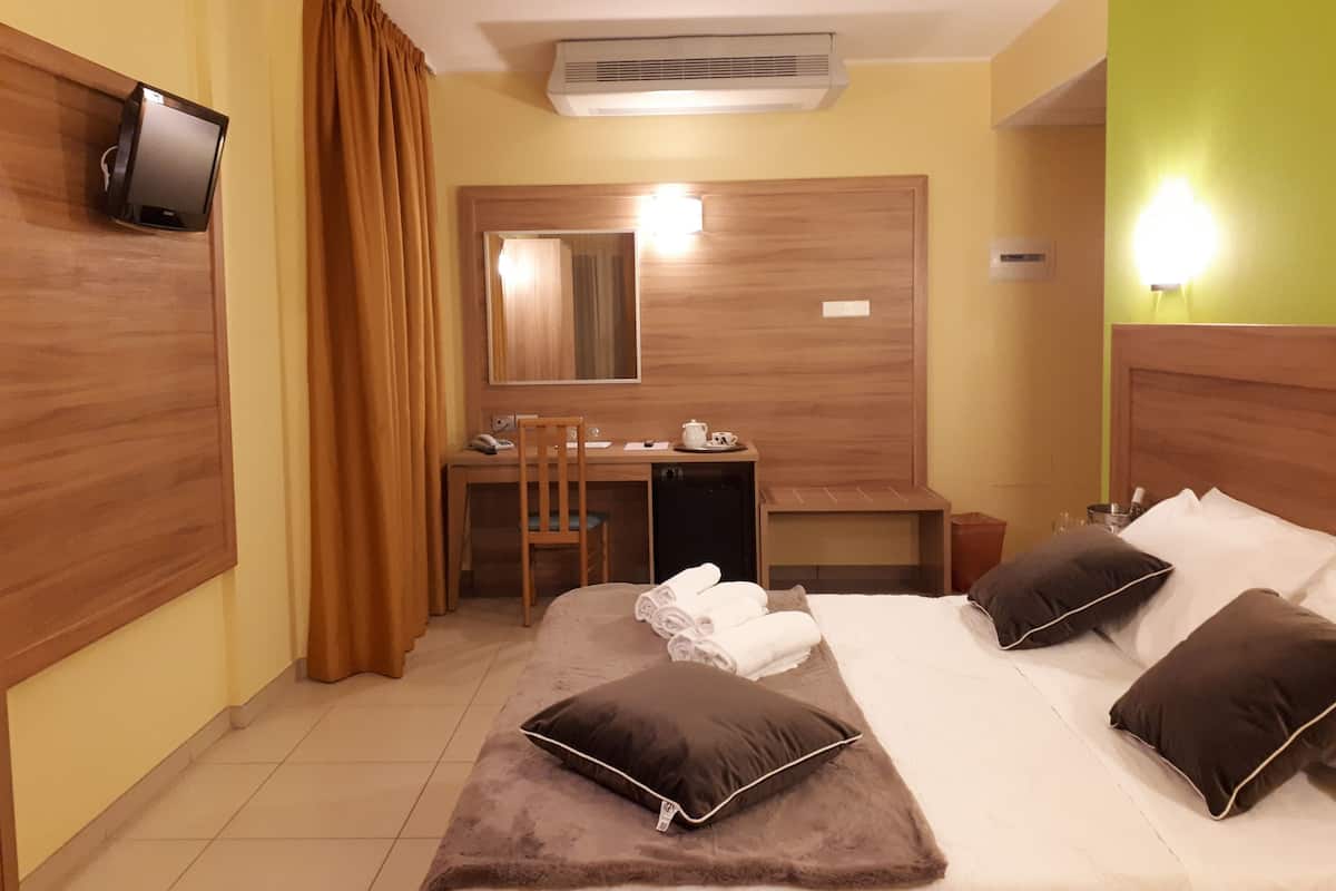 Quarto de hotel com cama, escrivaninha, cadeira, televisão e ar condicionado.