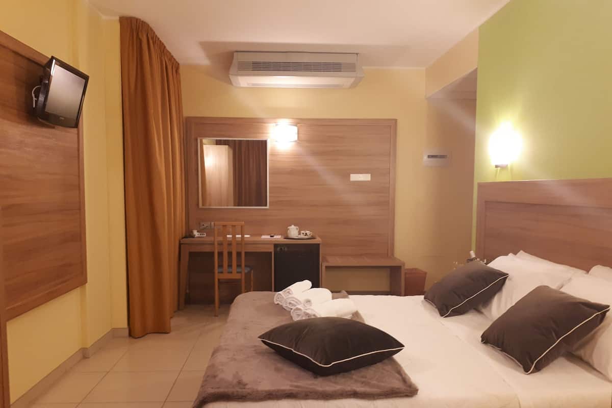 Quarto de hotel com cama, escrivaninha, cadeira, ar condicionado, televisão e espelho.