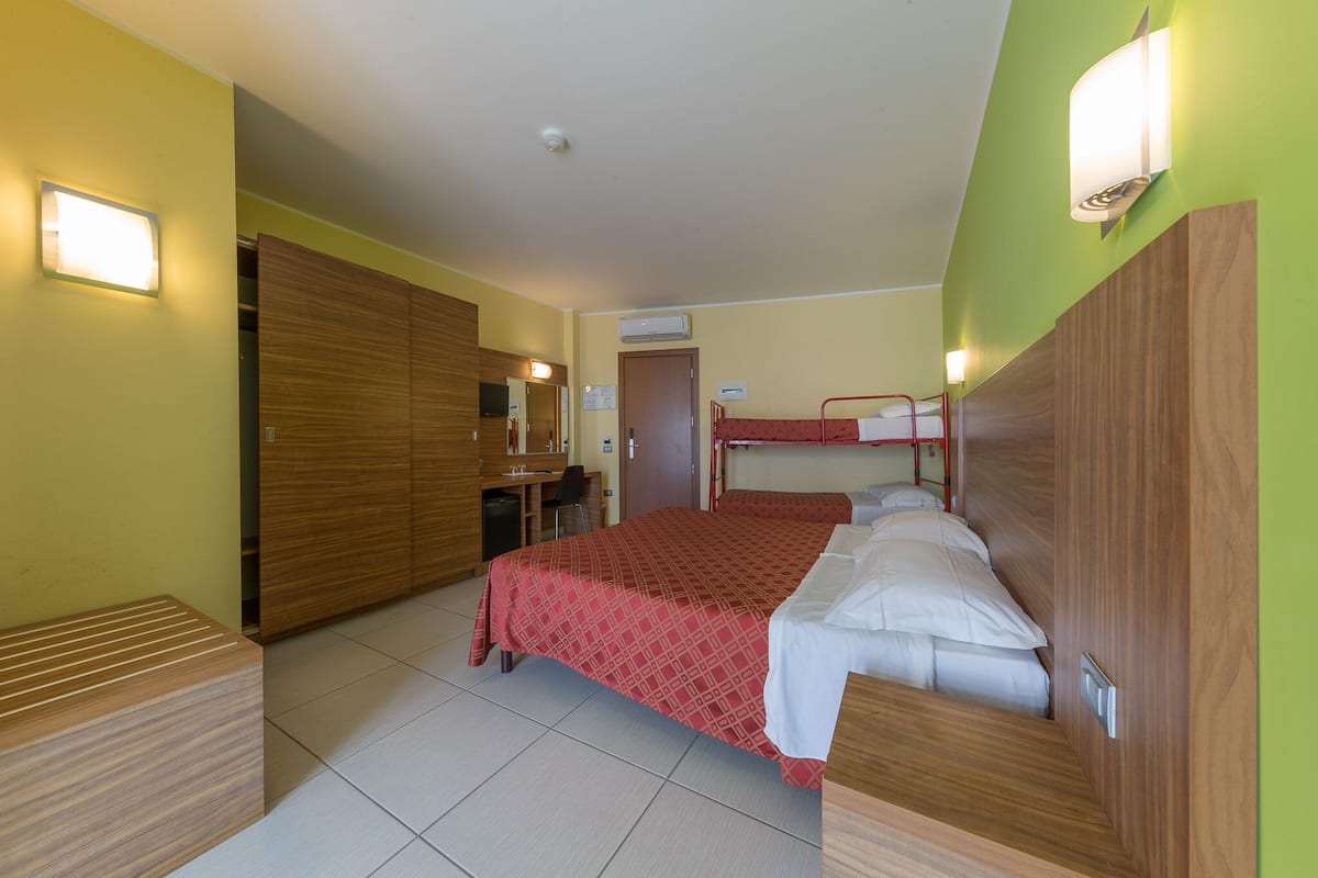 Quarto de hotel com beliche, escrivaninha, cadeira e guarda-roupa.