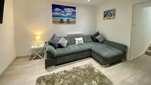 Uma sala de estar moderna com um sofá seccional cinza, um tapete fofinho e uma pintura de uma paisagem praiana.