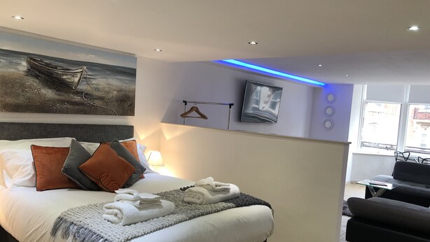 Quarto de hotel moderno com uma cama grande, um quadro de um barco na parede, uma televisão e um sofá.