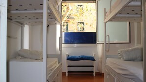 Um vagão de trem com beliches, uma janela com vista para edifícios e uma pequena mesa no centro.