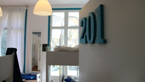 Quarto com cama de solteiro, escrivaninha e o número 201 grande na parede.