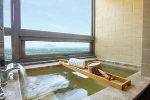 Área de spa com hidromassagem, acessórios de banho em madeira e janela com vista para a cidade.