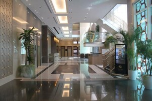 Um hall de hotel moderno com piso lustroso, balcão de recepção e escada para andares superiores.