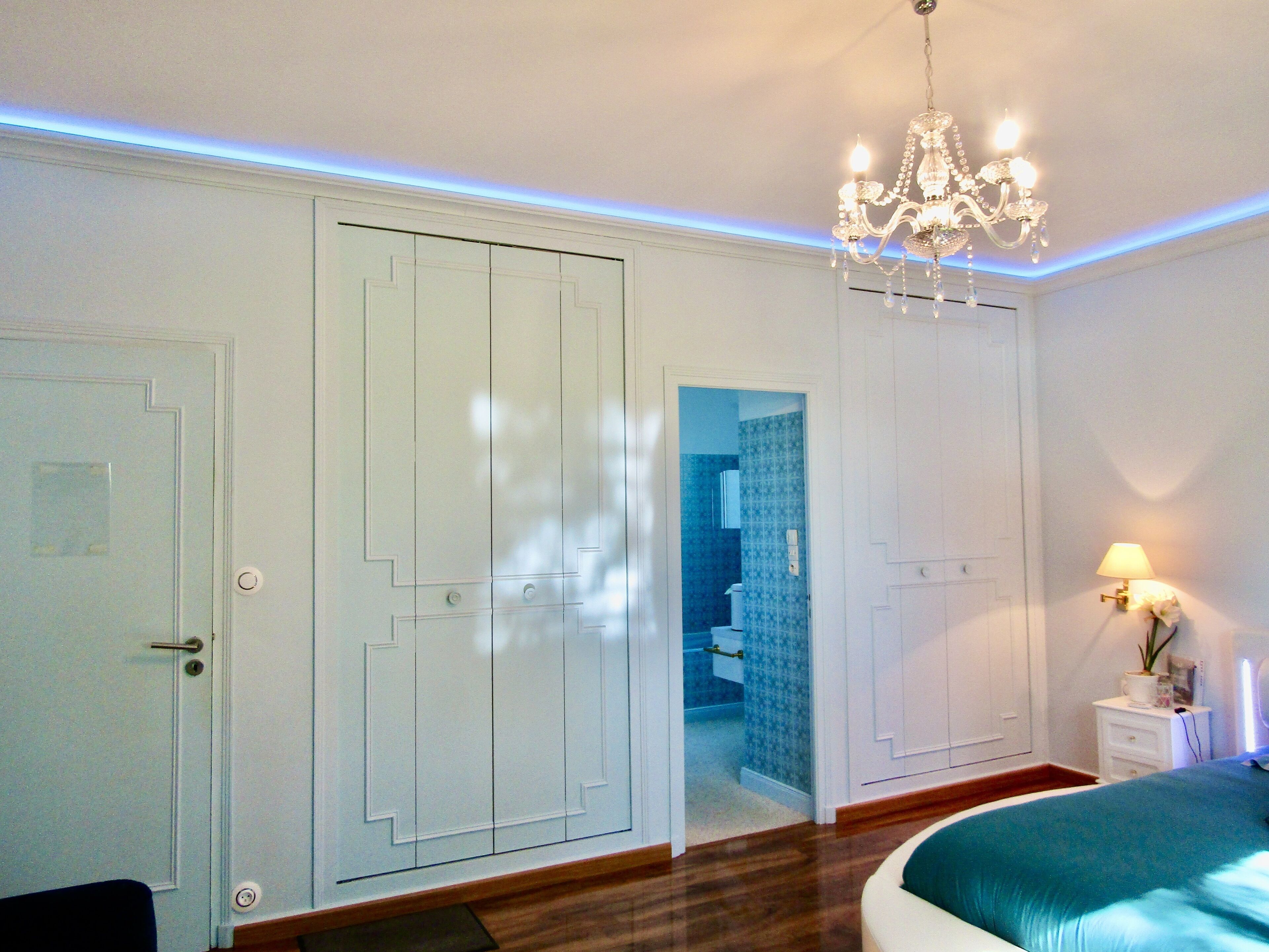 Quarto com cama grande, um lustre e um banheiro visível por uma porta aberta.