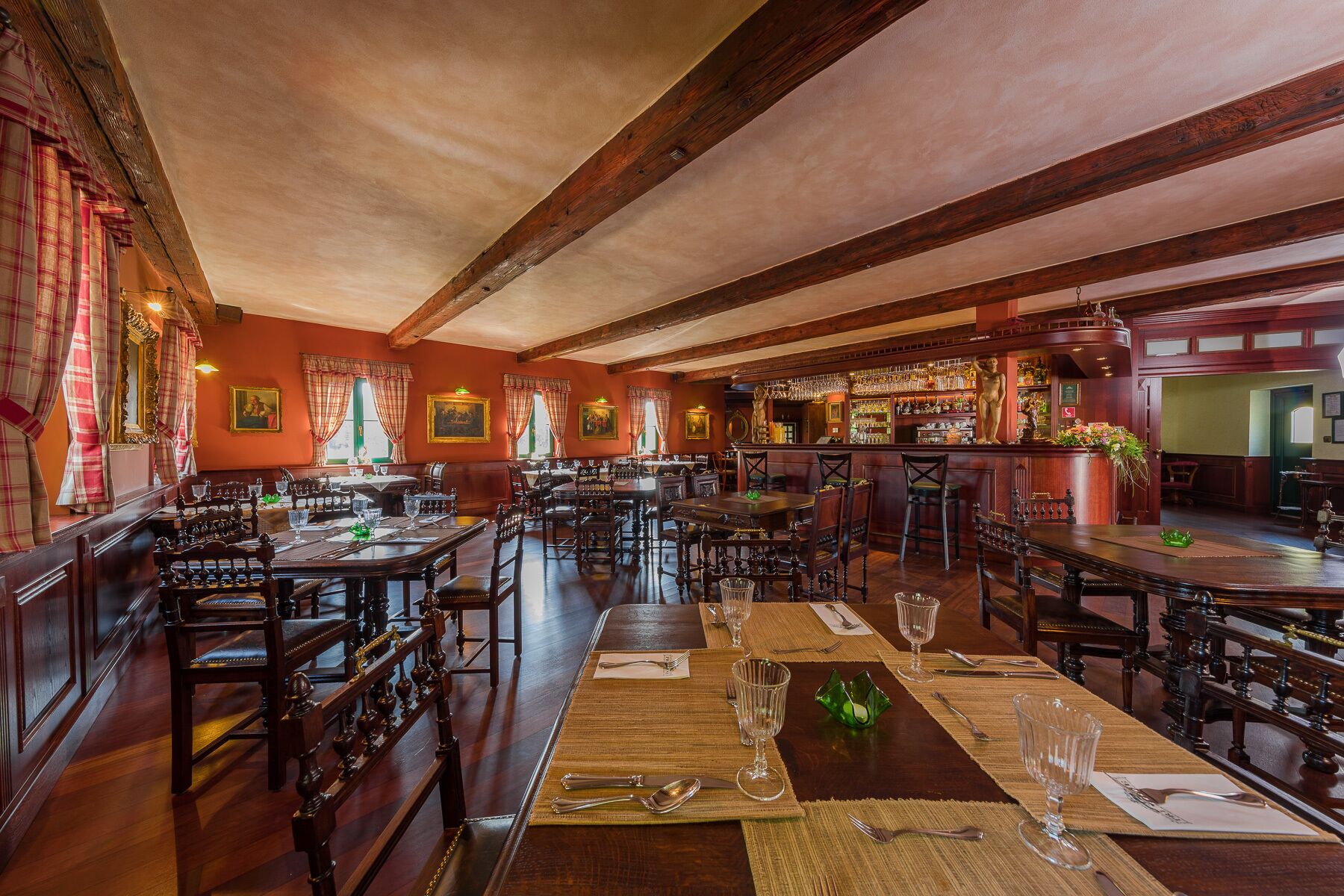Restaurante com mobiliário de madeira, área de bar e paredes vermelhas.