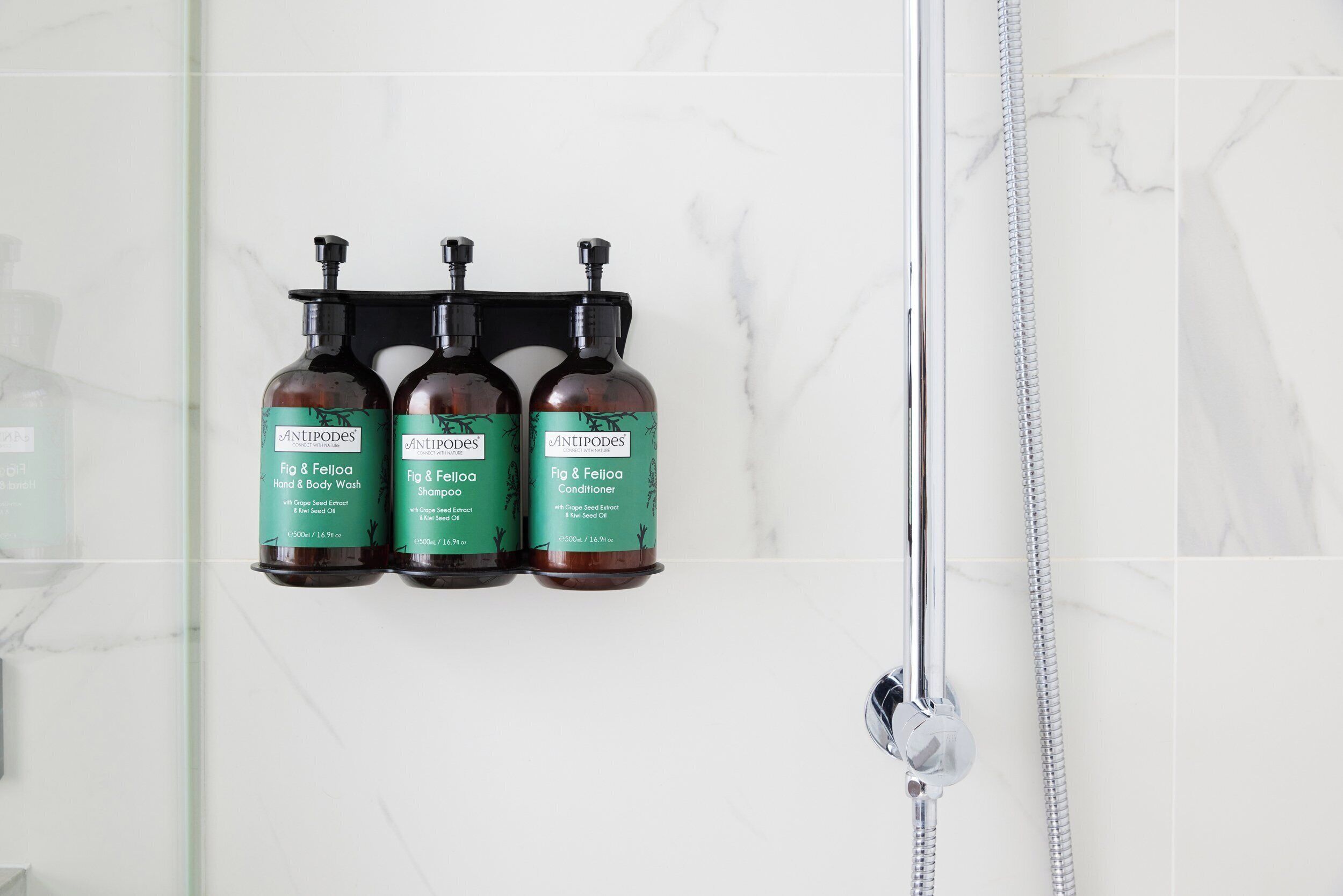 Casa de banho com três embalagens de gel de banho e corpo, champô e condicionador Fig & Feijoa, num dispensador fixado na parede.