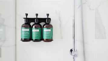 Casa de banho com três embalagens de gel de banho e corpo, champô e condicionador Fig & Feijoa, num dispensador fixado na parede.