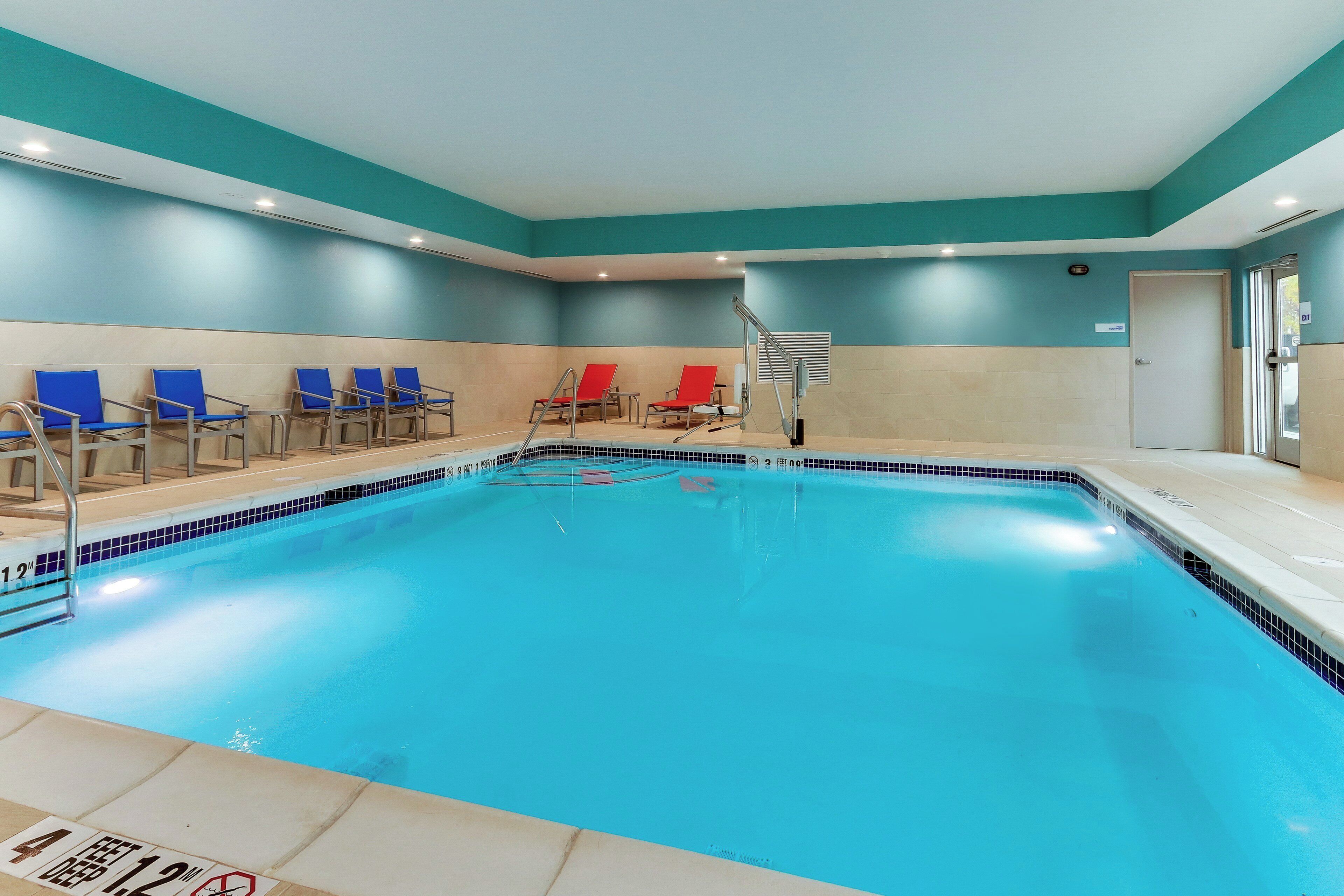 Piscina com azulejos azuis, plataforma de mergulho e várias cadeiras.