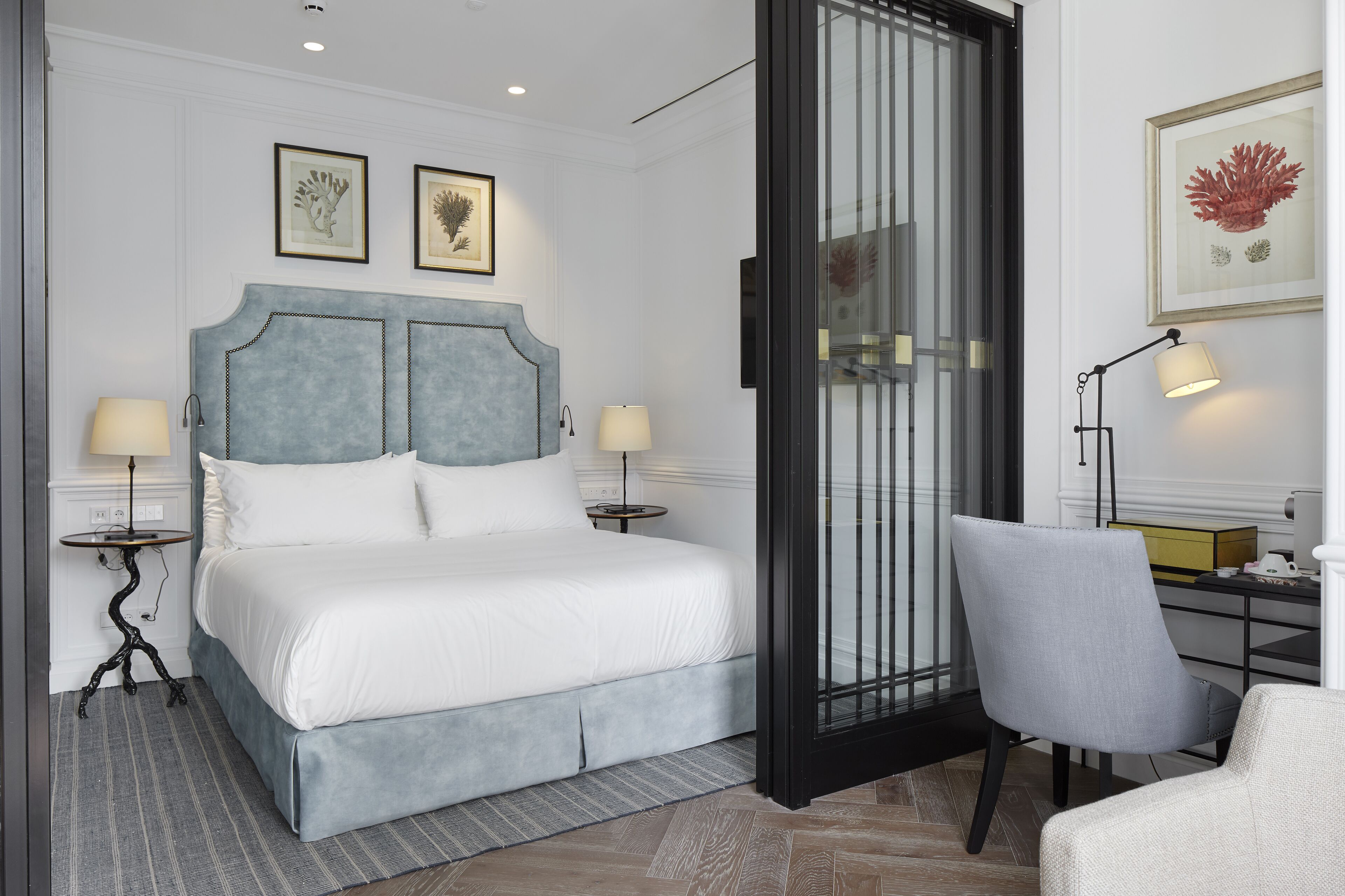 Quarto de hotel com cama, mesas de cabeceira, escrivaninha e cadeira, e obras de arte nas paredes.