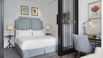 Quarto de hotel com cama, mesas de cabeceira, escrivaninha e cadeira, e obras de arte nas paredes.
