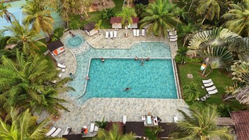 Uma piscina retangular grande rodeada por espreguiçadeiras e palmeiras.