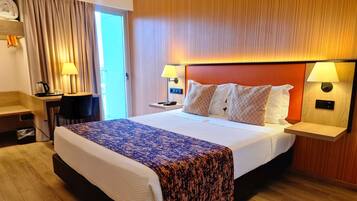 Quarto de hotel com uma cama grande, abajures, uma escrivaninha com cadeira e uma pequena mesa.