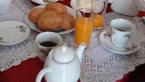 Mesa posta para o café da manhã com croissants, suco de laranja, café e chá, sobre uma toalha de renda.