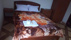 Cama com colcha florida, dois travesseiros brancos e uma pequena bandeja branca com toalha e chave.