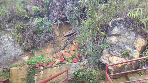 Uma escadaria de madeira com grades vermelhas descendo para uma área rochosa com plantas em vasos.