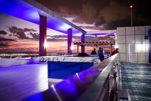 Terraço no telhado com vista para o pôr do sol, área de piscina e espaço coberto para sentar.