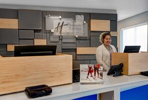 Uma receção com o letreiro Holiday Inn Express, um quiosque digital e um folheto de boas-vindas.