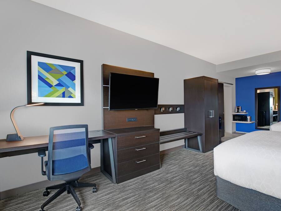 Quarto de hotel com escrivaninha, cadeira, televisão, guarda-roupa e cama.