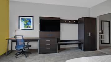 Quarto de hotel com escrivaninha, cadeira, televisão, guarda-roupa e uma cama.