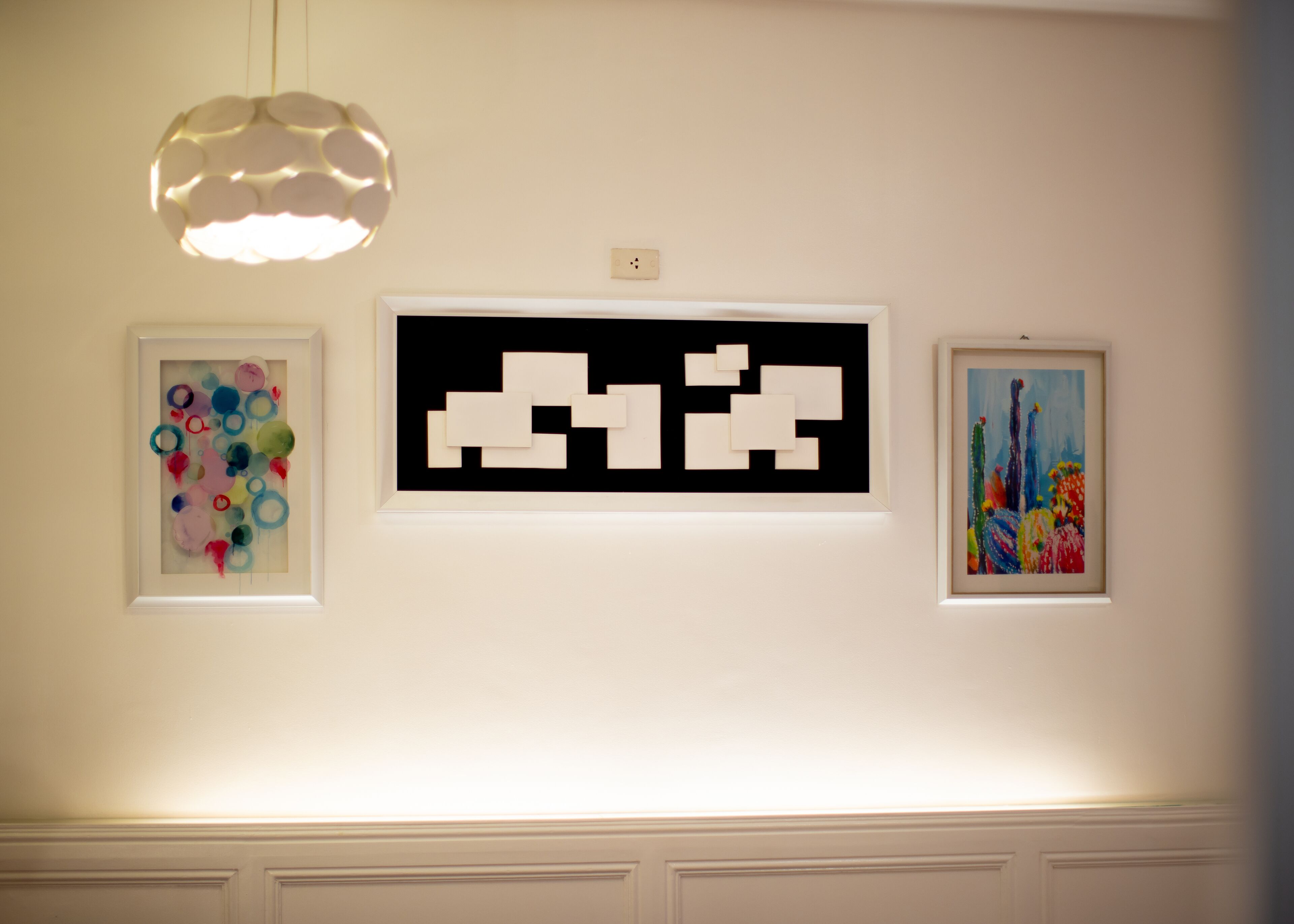 Uma parede com uma galeria de três obras de arte emolduradas, um aplique e uma tomada.