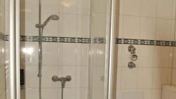 Um chuveiro envidraçado com chuveiro manual e torneira na parede.