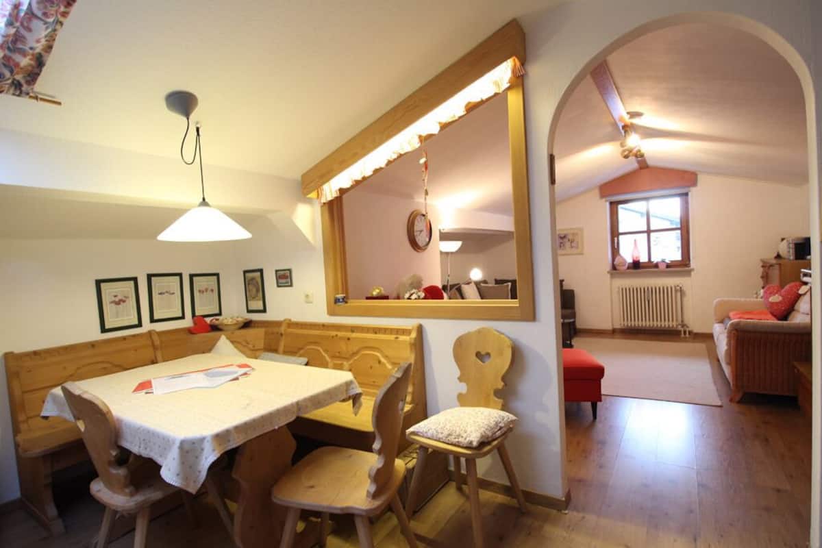 Uma sala de jantar com uma mesa e cadeiras de madeira, um ventilador de teto e um espelho grande acima da mesa.