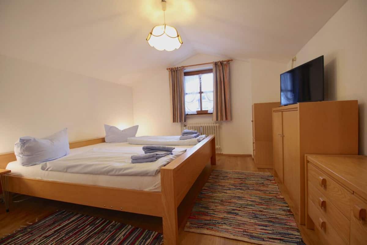 Quarto com cama de madeira, televisão sobre um móvel de madeira e janela com cortinas.