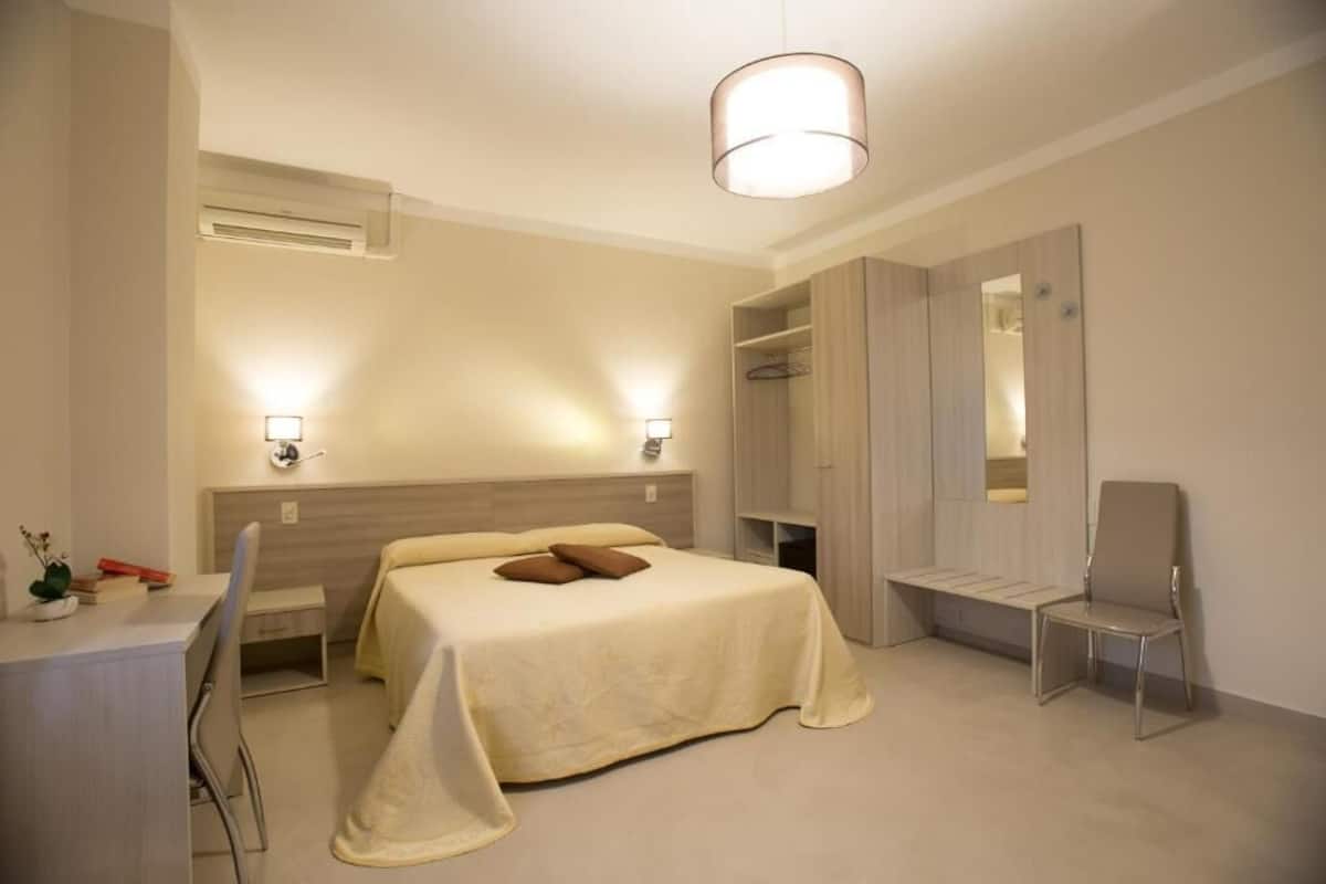 Quarto moderno com cama, mesas de cabeceira, escrivaninha e guarda-roupa.