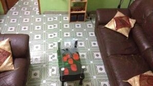 Sala de estar com piso estampado, sofá de couro marrom e uma mesinha com uma bolsa em cima.