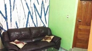 Uma sala de estar com um sofá de couro marrom, parede estampada e porta de madeira.