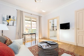 Uma sala de estar moderna com sofá, mesa de centro redonda, televisão de tela plana e uma área de jantar com cadeiras e mesa.