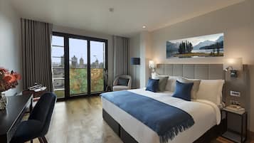 Quarto de hotel moderno com uma cama grande, uma escrivaninha e uma cadeira. Vê-se uma vista da cidade pela janela.