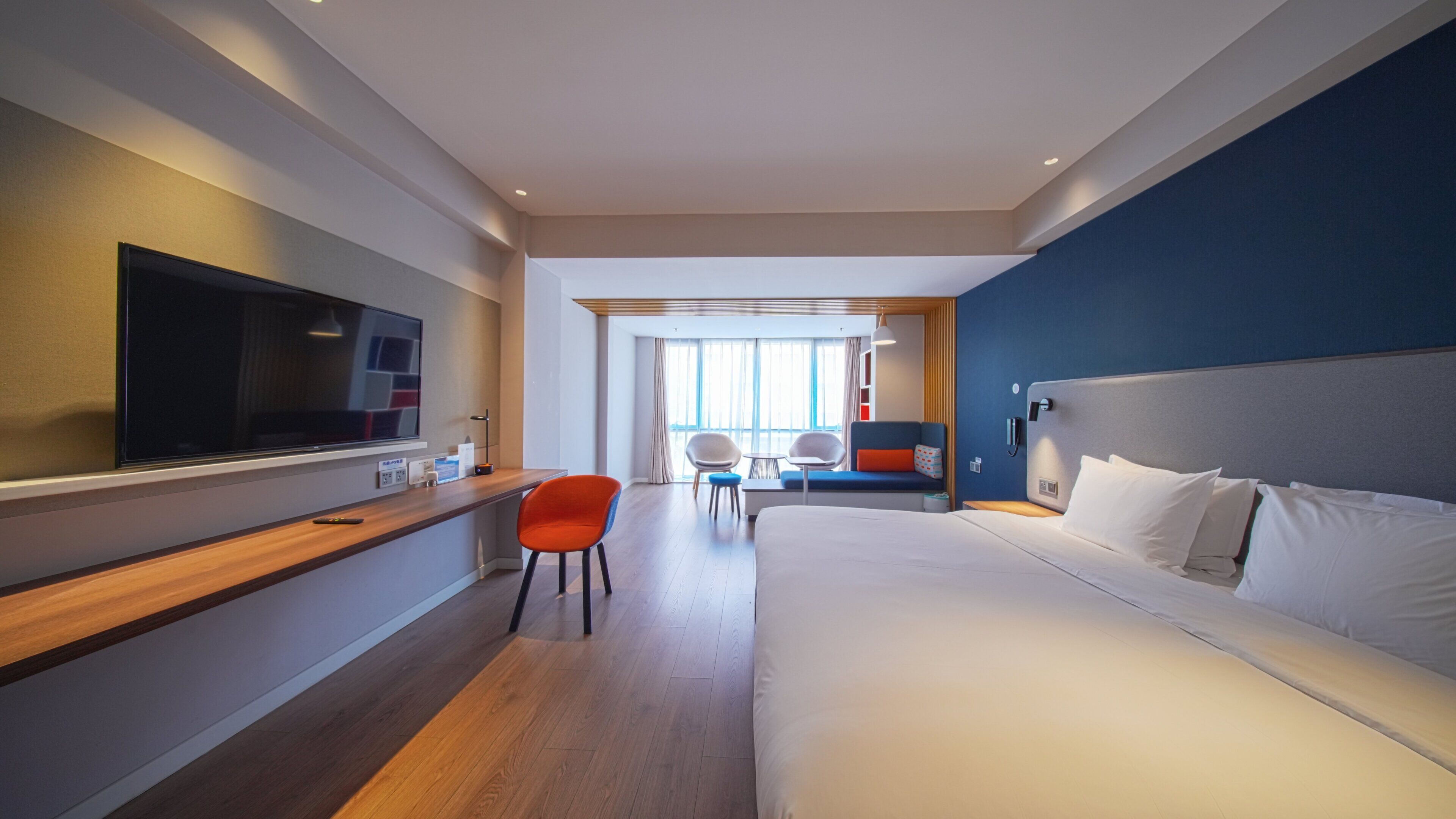 Quarto de hotel com cama, secretária com televisão, cadeira e vista para o exterior.