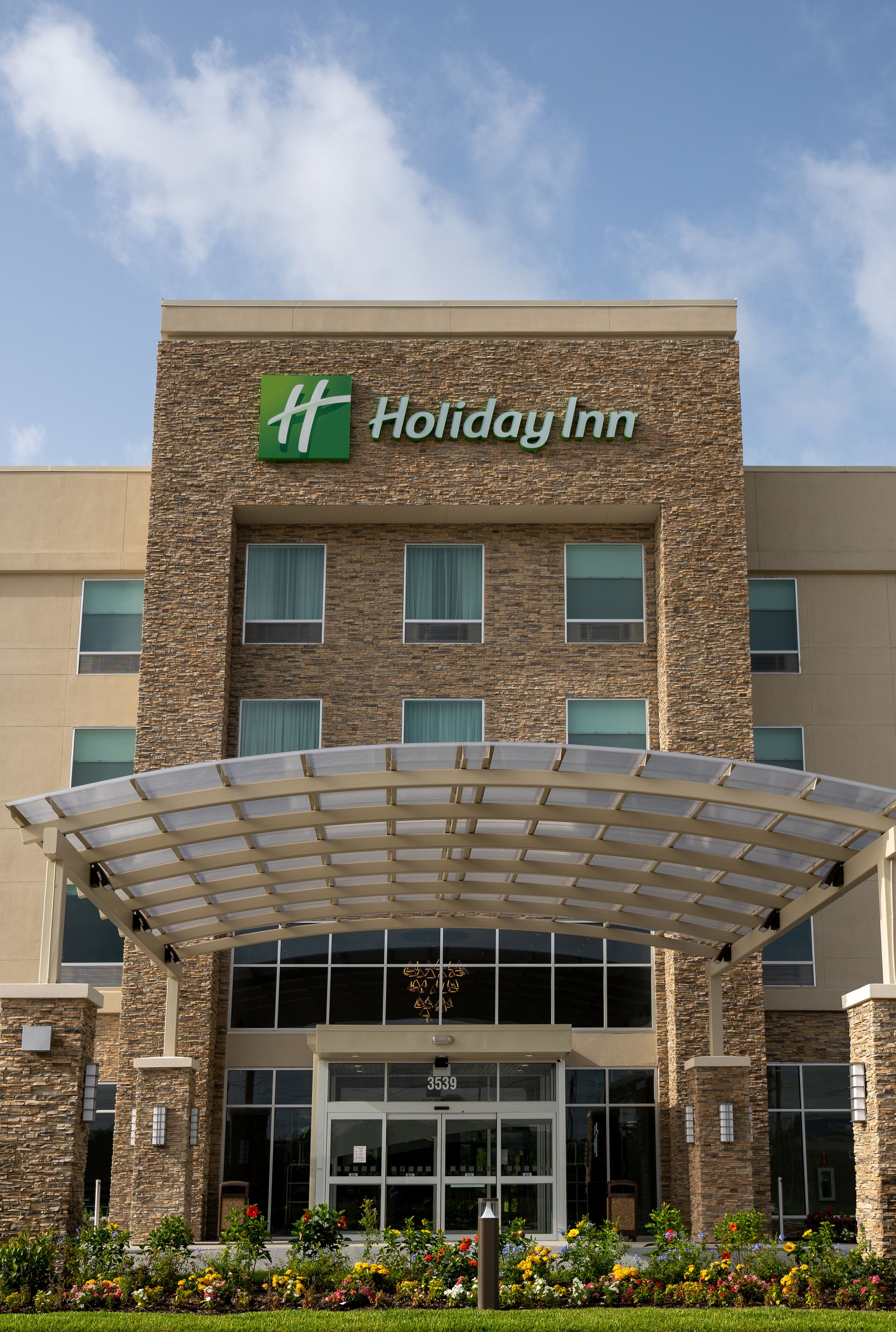 Um hotel Holiday Inn com fachada de pedra, janelas grandes e entrada coberta.