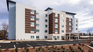 Um hotel de vários andares com design moderno, apresentando uma combinação de painéis brancos e castanhos, uma entrada coberta e um estacionamento.
