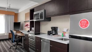 Cozinha moderna equipada com micro-ondas, cafeteira e frigorífico. Possui área de refeições com mesa e cadeiras, e uma televisão fixada na parede.