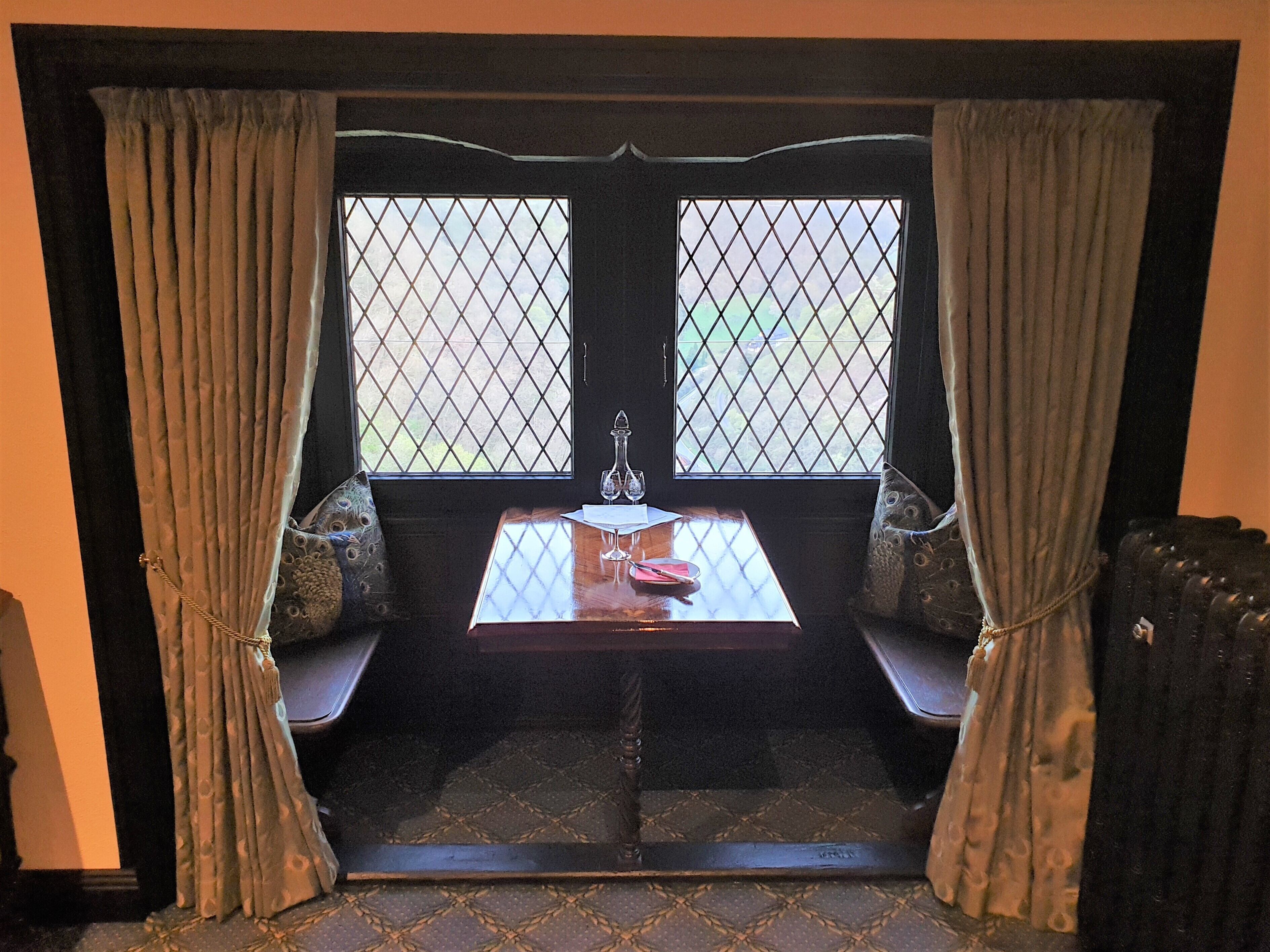 Um quarto com janela, uma mesa com um vaso e um banco com almofadas.