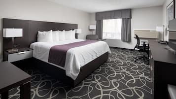 Quarto de hotel com uma cama grande, duas mesas de cabeceira com luminárias, uma escrivaninha com cadeira, uma televisão e uma janela com cortinas.