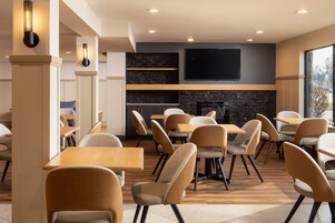 Interior moderno de restaurante com mesas e cadeiras de madeira, parede de pedra e uma televisão de tela plana acima da área de estar.