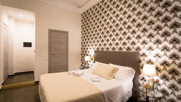Quarto de hotel com uma cama grande, mesa de cabeceira, abajur e papel de parede estampado.