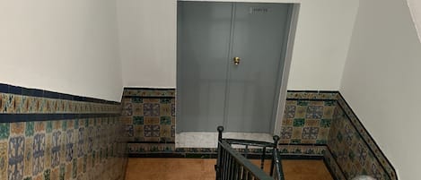 Uma escada com corrimão, uma porta com a inscrição 'LAVANDERIA' e uma placa de 'SILENCIO' acima.