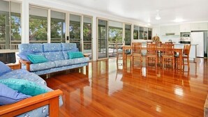 Uma sala de estar espaçosa com piso de madeira, um sofá azul com almofadas estampadas, uma mesa de jantar com cadeiras e uma área de cozinha com eletrodomésticos.