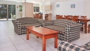 Sala de estar com sofá e poltronas estampadas, mesa de centro de madeira e canto de jantar com cadeiras e mesa de madeira.