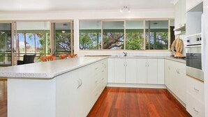 Uma cozinha moderna com armários brancos, bancada de madeira e grandes janelas com vista para árvores.