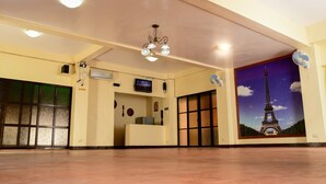 Um saguão de hotel com balcão de recepção, um candelabro, um aparelho de ar condicionado, uma televisão e um mural grande da Torre Eiffel.