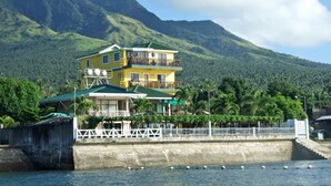 Um edifício de dois andares com varandas, localizado à beira-mar com uma montanha ao fundo.