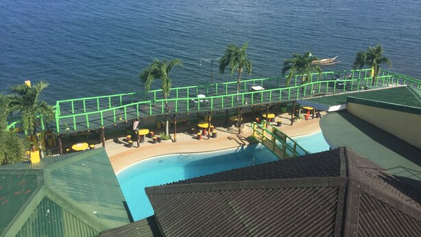Área da piscina com vista para o oceano, deck verde com assentos e palmeiras.