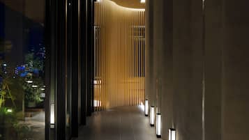 Um corredor moderno com parede de ripas de madeira, iluminação embutida e vista para a cidade através de grandes janelas.